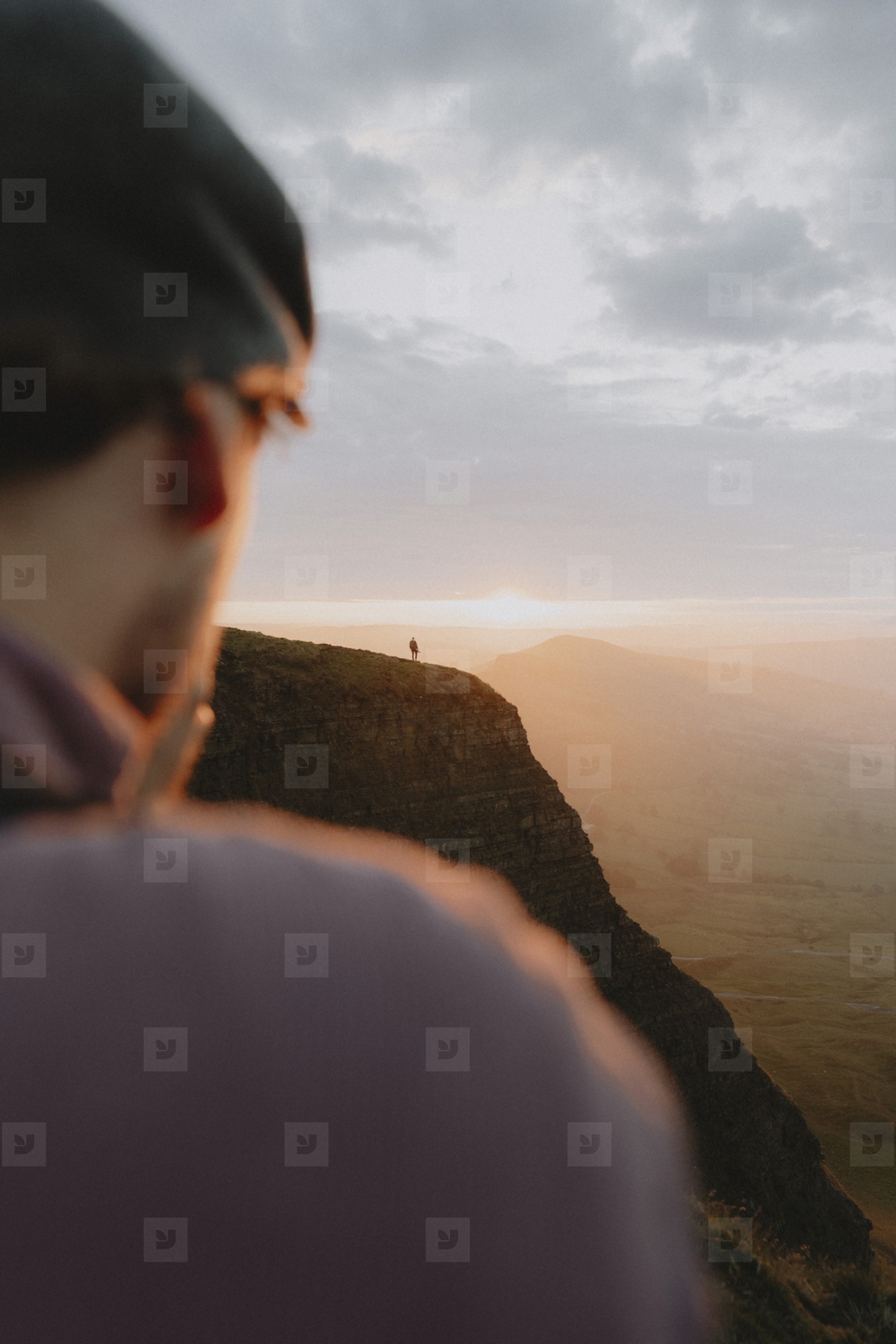 Over the shoulder view hiker at the edge of rugged hilltop at sunrise ...