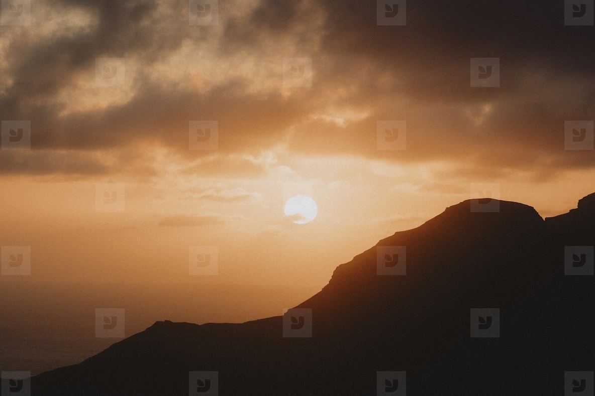 Sunset in orange sky above silhouetted cliffs and sea stock photo ...